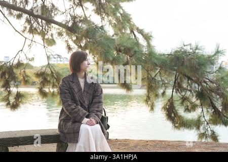 Autumn lake woman. She sits by a pond on a wooden pier in autumn and ...