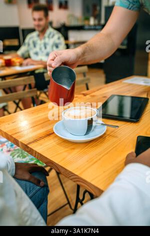 A person pouring hot creamy milk into a cup of coffee, making coffee ...