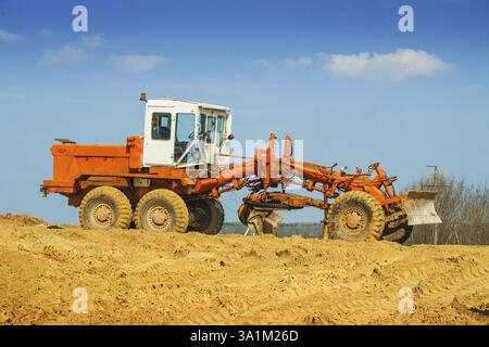 old roadworking tractor standing on pile of sand on background of sky ...