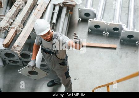 Making gesture by hands. Young factory worker in grey uniform Stock ...