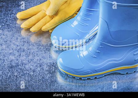 Waterproof rubber boots leather safety gloves on metallic background ...
