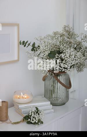Chest of drawers with candle and eucalyptus branches near light wall ...