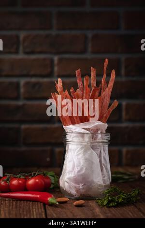 Thinly sliced cured meat arranged on rustic wooden board. Red chili ...