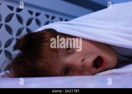 Afraid boy under blanket on bed at night Stock Photo - Alamy
