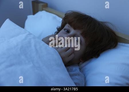 Scared boy lying in bed at night Stock Photo - Alamy