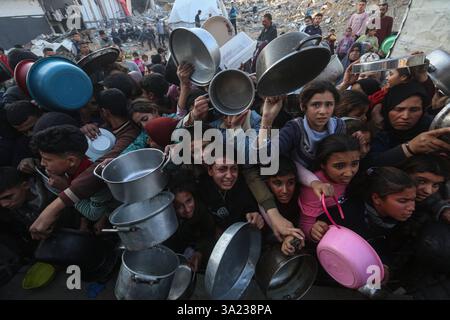 Displaced Palestinians queue to receive a share of food from a charity ...