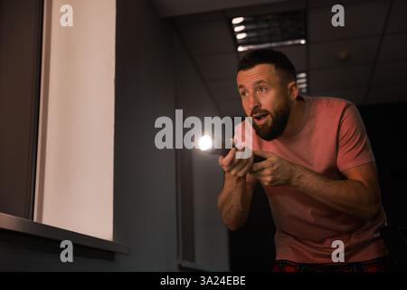 Fear of darkness. Scared man with flashlight sitting on bed in room at ...
