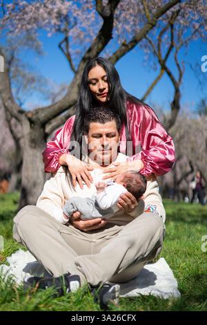 Happy latin parents holding their newborn child under a blooming tree ...