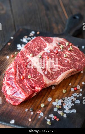 Thick, marbled ribeye steak resting on a rustic board, seasoned with ...