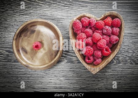 Round and heart-shaped bowls with juicy raspberries on wooden board ...