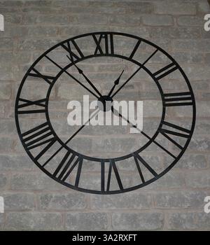 A large metal wire frame clock with roman numerals hangs on a grey ...