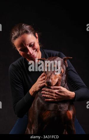 Portrait of a laughing woman and a Doberman dog touching her face with ...