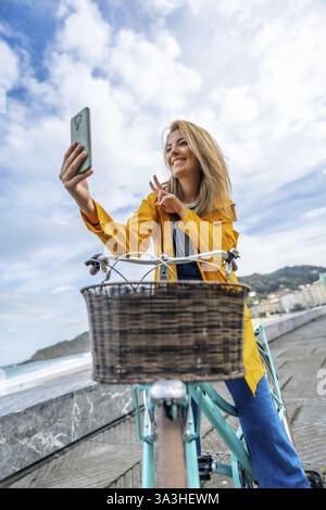 Young woman in yellow raincoat with rainbow umbrella against blue ...