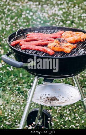 Chicken legs and merguez sausages cooking on a barbecue in the garden ...