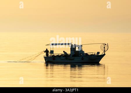 Traditional Cypriot caique fishing boat setting its nets at sunset ...