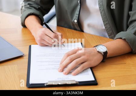 Client signing notarial document at wooden table in office, closeup ...