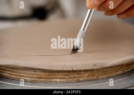 Using a sharp pottery carving knife to cut out a perfect round shape ...