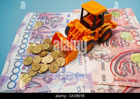 Excavator with tenge coins on the background of tenge banknotes of ...