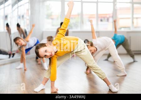 Positive juvenile girl engaged in breakdancing in training room with ...