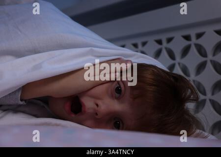 Afraid boy under blanket on bed at night Stock Photo - Alamy