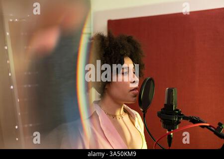 Black female singer performing song against microphone with pop filter ...