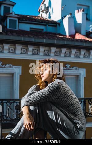 Hispanic woman sits on a balcony reading a book, enjoying daylight in ...