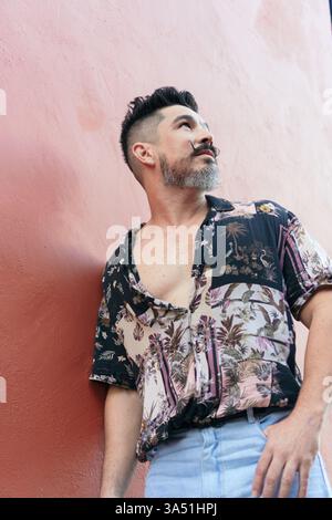 Low angle of calm thoughtful bearded guy in casual clothes standing on ...