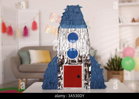 Bright pinata in shape of rocket on table in festive decorated room ...