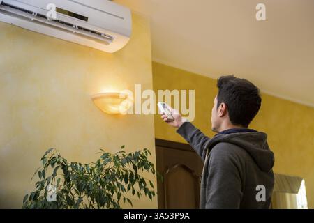 Young man switching air conditioner with remote controller in living ...