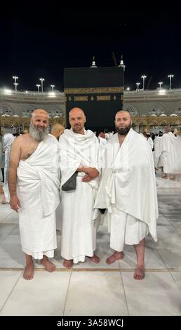Three Muslim men in Ihram clothing standing in front of the Kaaba ...