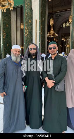 Three Muslim men in Ihram clothing standing in front of the Kaaba ...
