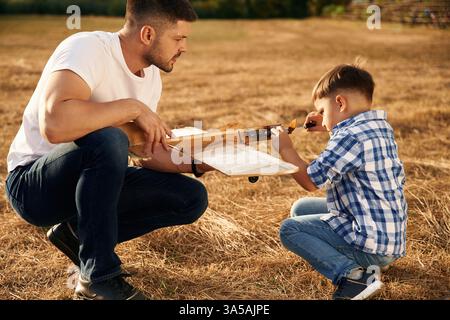 Focused by fixing the toy. Father and son are with wooden plane on the ...