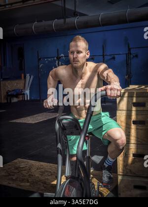 Hunky muscular blond male bodybuilder exercising on stationary bike in ...