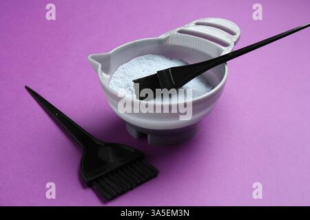 Bowl of hair bleaching powder, brushes and gloves on purple background ...