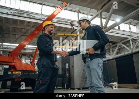 Friendly handshake. Two male factory workers are in the warehouse Stock ...
