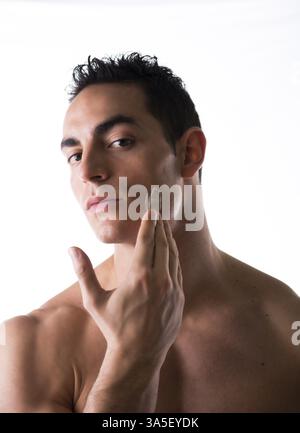 Handsome man applying moisturizing cream onto his face on grey ...