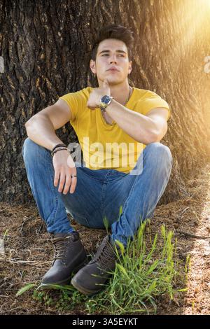Attractive young man in park resting against tree Stock Photo - Alamy