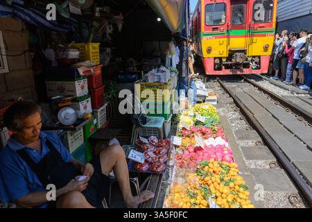 A local Thai market vendor sits with his fruits as a train approaches ...