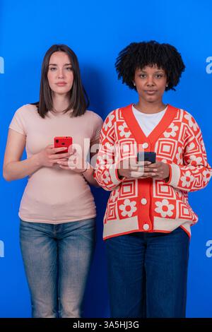 Serious friends women using smartphones against a bright blue ...