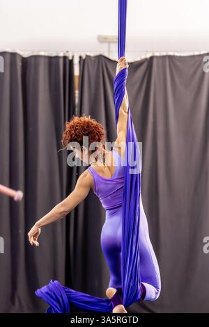 Female acrobat executing an aerial pose, hanging upside-down with red ...