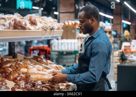 Supermarket worker is standing near bread products Stock Photo - Alamy
