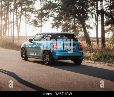 Blue Mini Cooper parked on an downhill forest road. Three quarter front ...