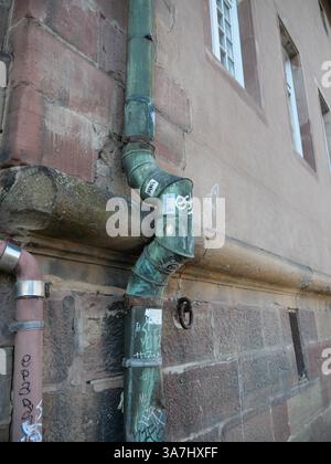 The downpipe of a roof drainage system is shaped around a stone ledge ...