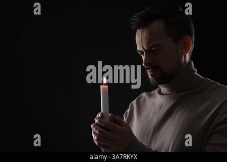 Sad man with burning candle crying on black background, space for text ...