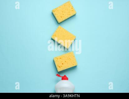 A bottle of dish washing, sponges, utensils on a wooden pastel color ...
