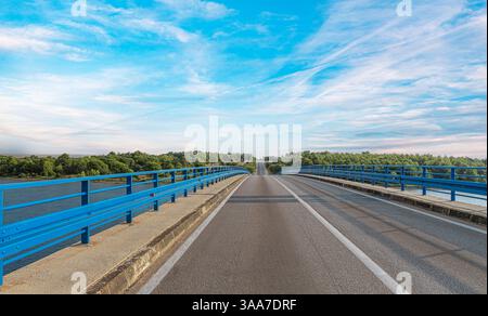 A long, straight bridge stretches over a body of water under a bright ...