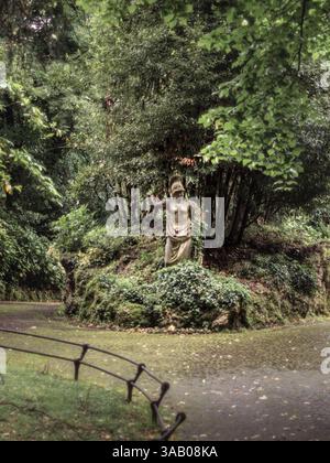 A moss-covered stone statue stands in a garden, weathered by time and ...