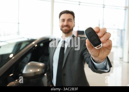 Happy salesman with key near new blue car in salon Stock Photo - Alamy
