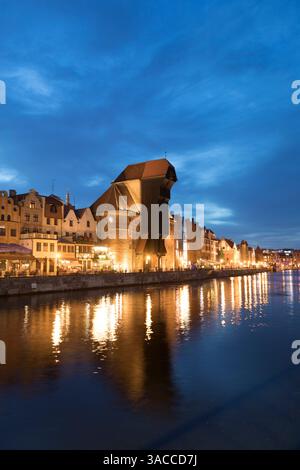 Waterfront tenements and crane reflected on Motlawa river at dusk ...