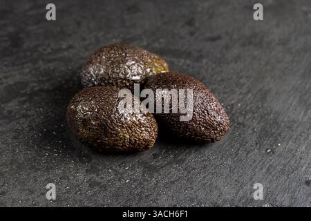wet avocado fruits on a black slate, ripe avocado fruit in drops of ...